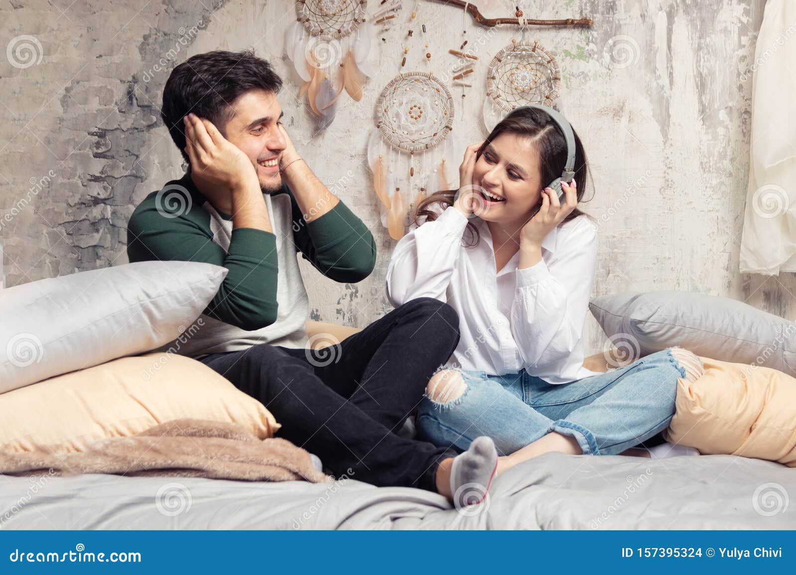 Loving Couple Listening To Music In Headphones Sitting On The Bed