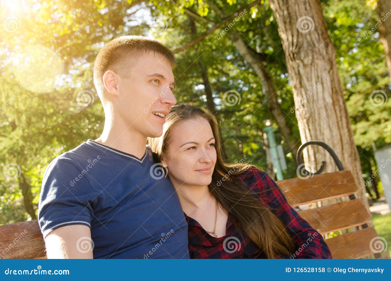 Loving Couple Sitting On Bench In Park Looking In One Direction Stock