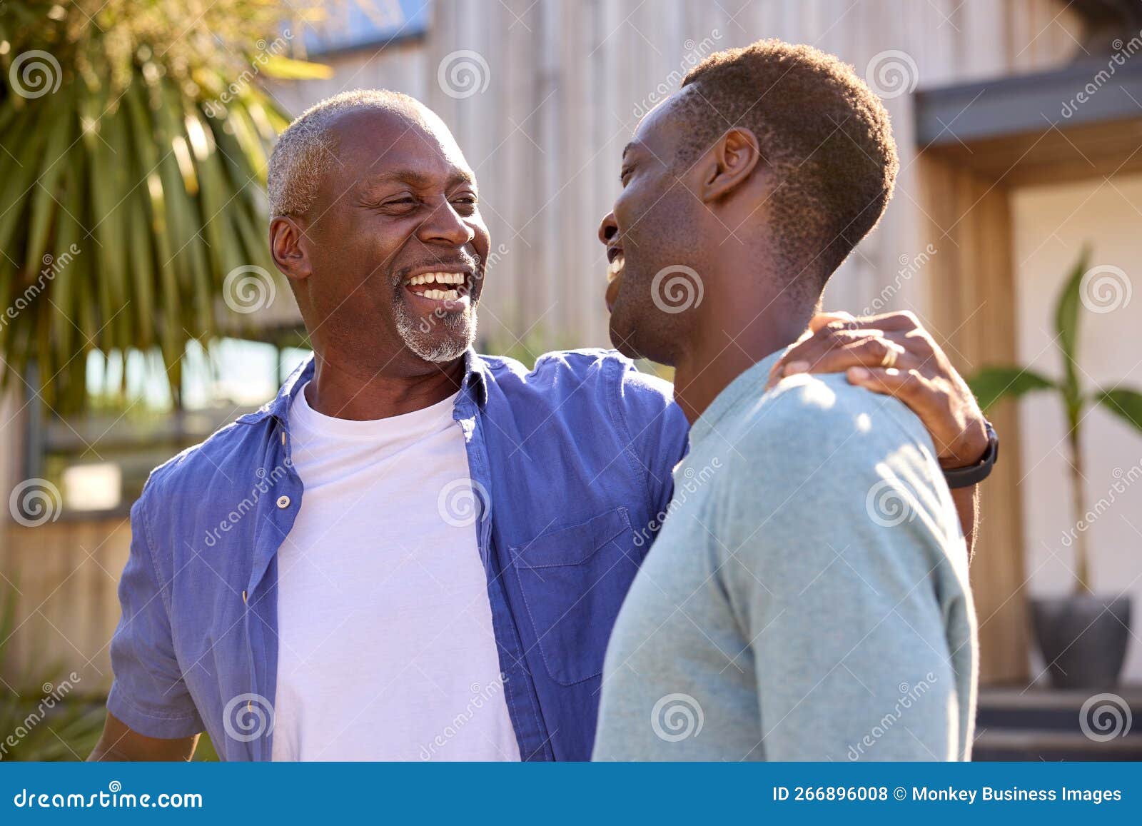 Loving Senior Father With Adult Son Standing Outside House Laughing
