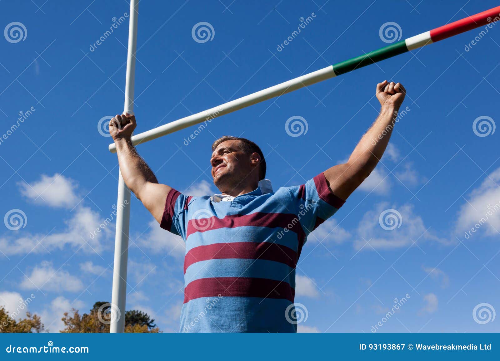 Low Angle View of Smiling Rugby Player with Arms Raised Against Blue ...