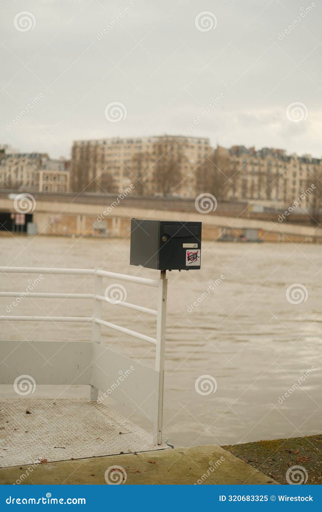 Mailbox on a Metal Railing in Front of a Lake with a Blurred Urban ...