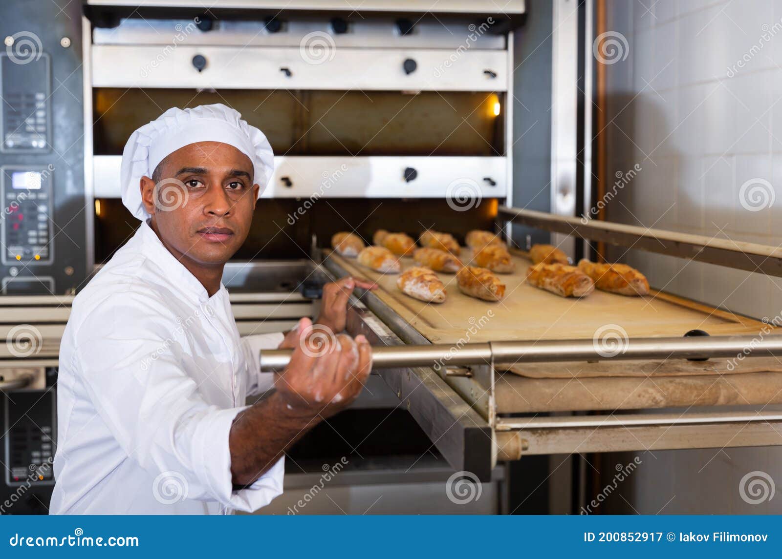 Male Bakery Worker Pulls Bread Pan Out of Oven Stock Image - Image of ...