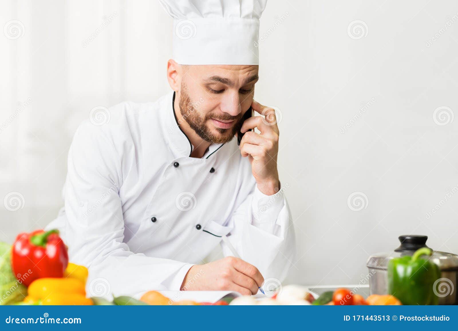 Male Chef Talking on Cellphone Taking Notes Standing in Kitchen Stock ...