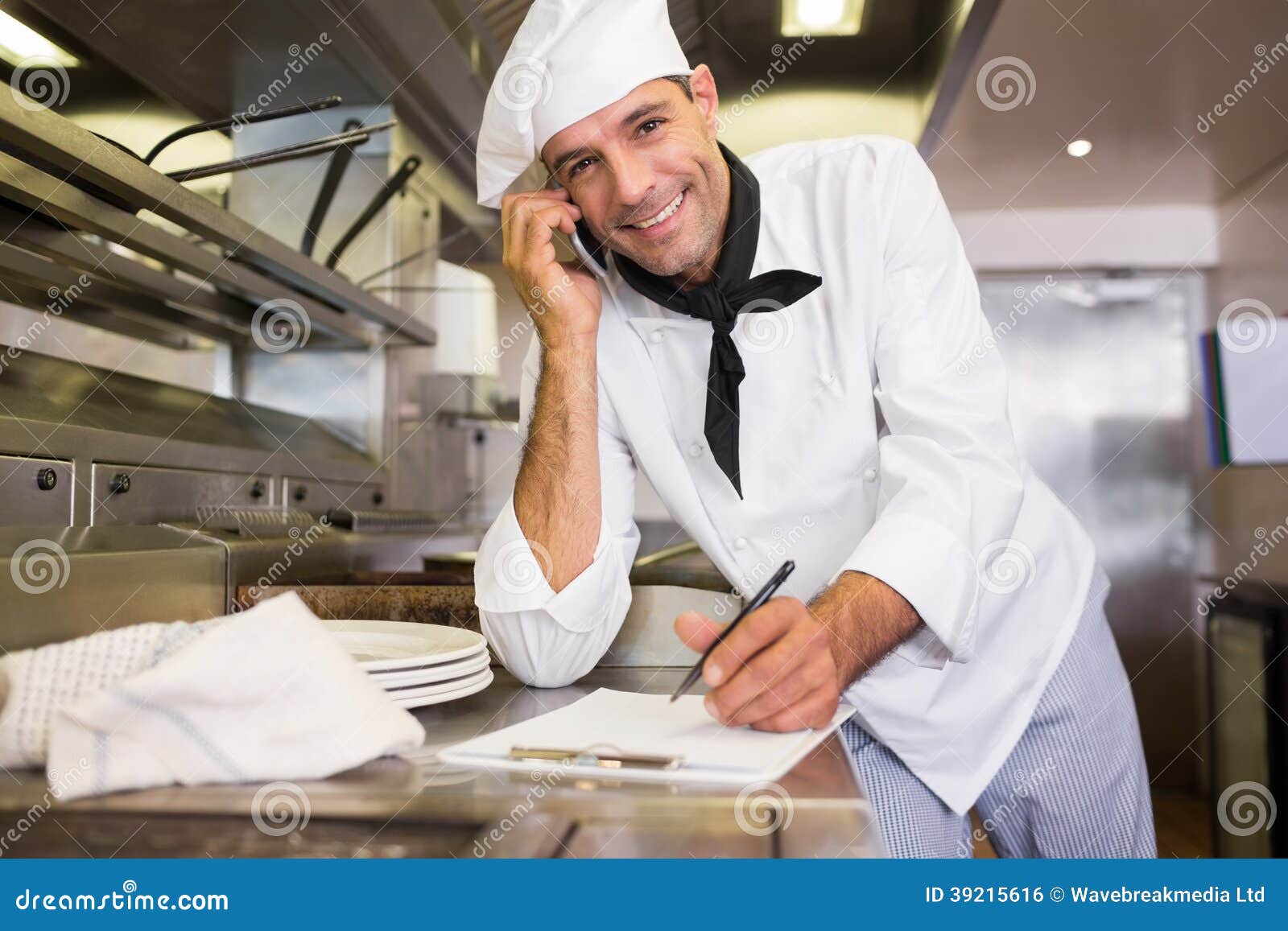 Male Cook Writing on Clipboard while Using Cellphone in Kitchen Stock ...