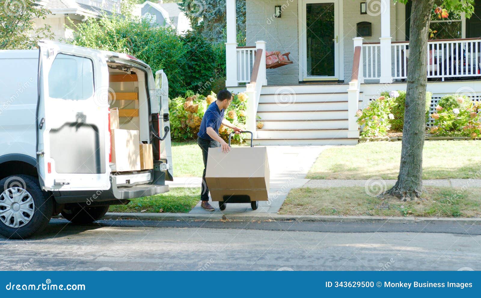Male Courier Using Trolley To Deliver Package from Van To House Stock ...