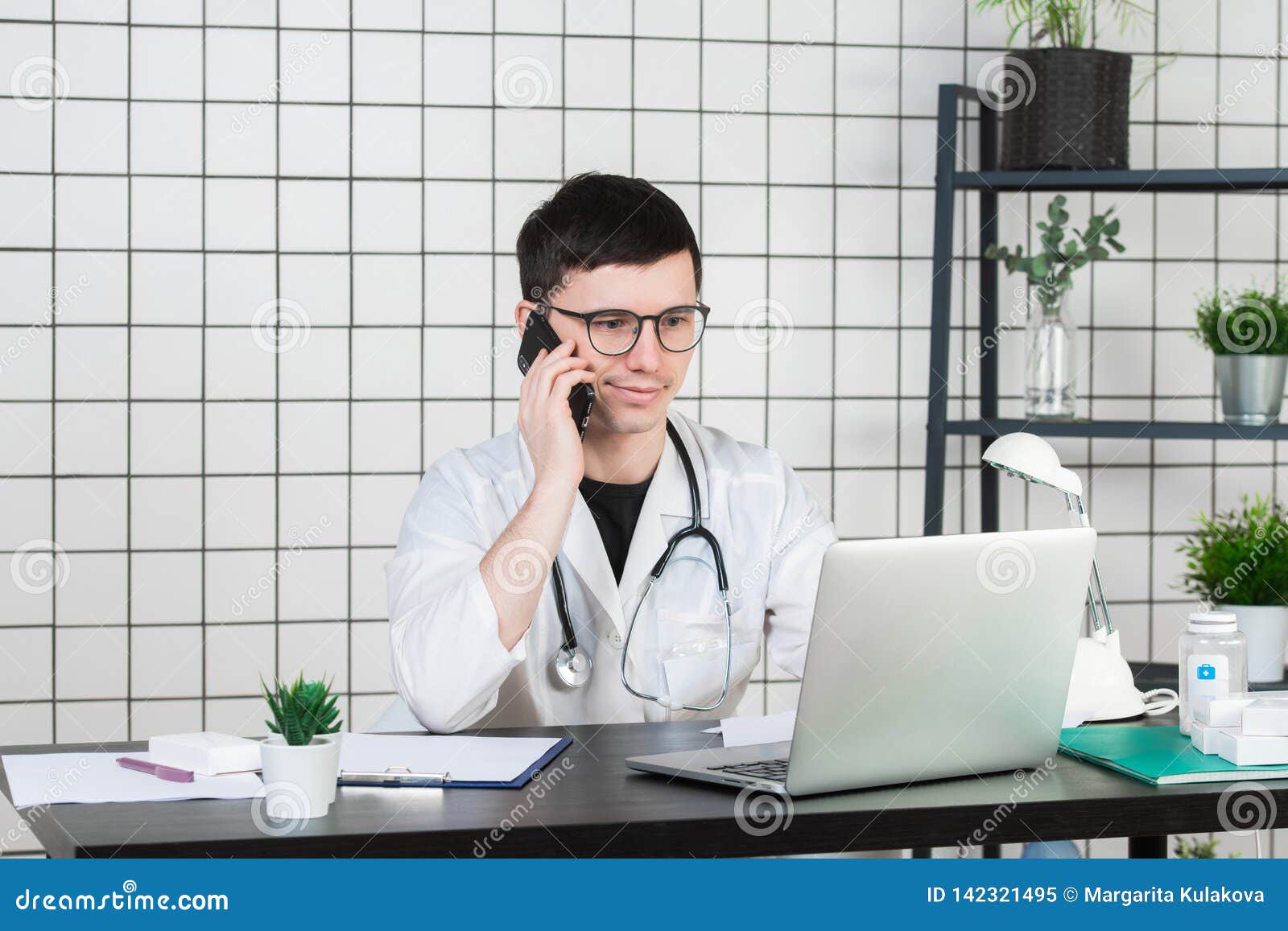 Male Doctor Using Telephone while Working on Computer at Table in ...