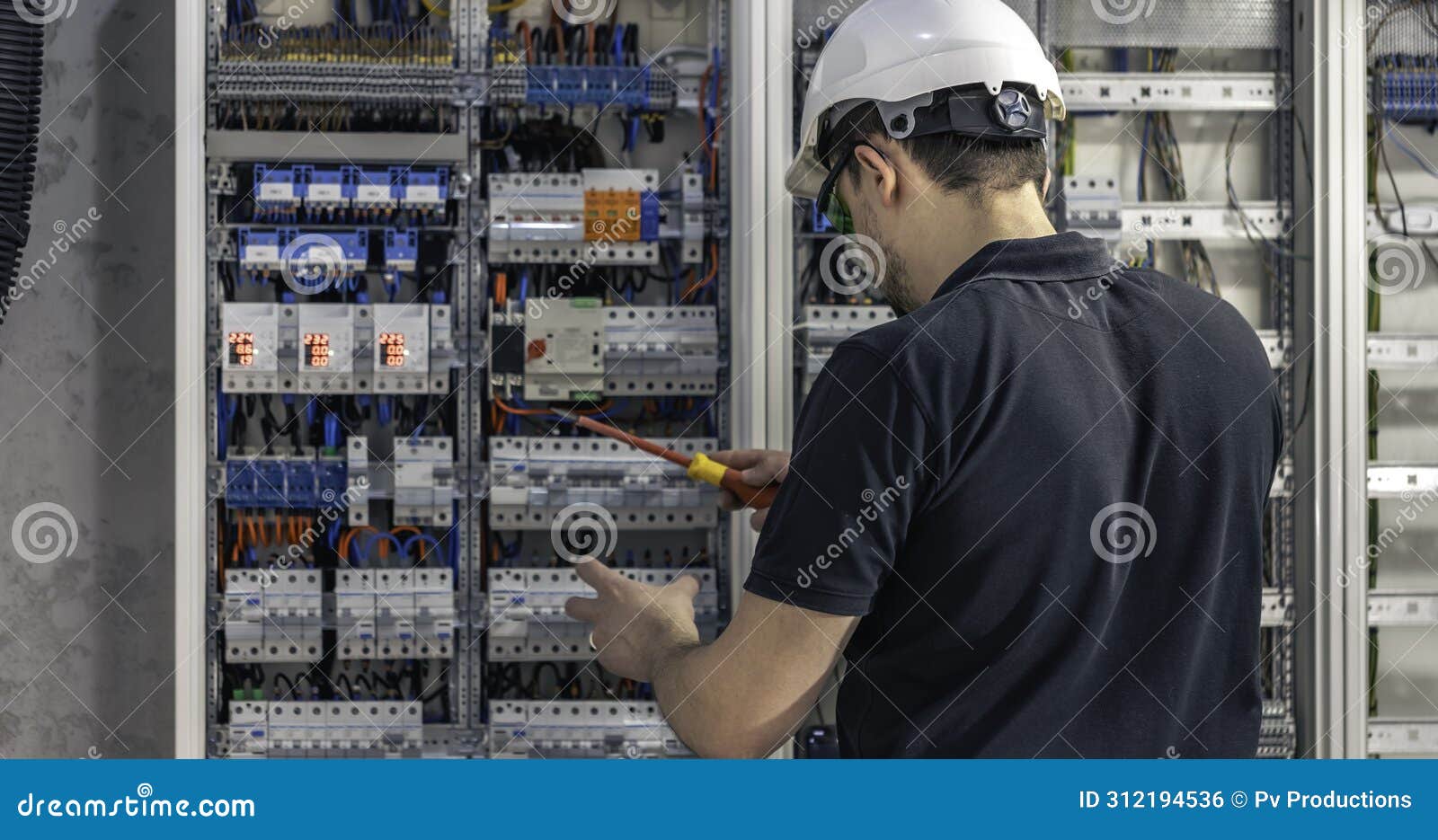A Male Electrician Works in a Switchboard Using an Electrical ...