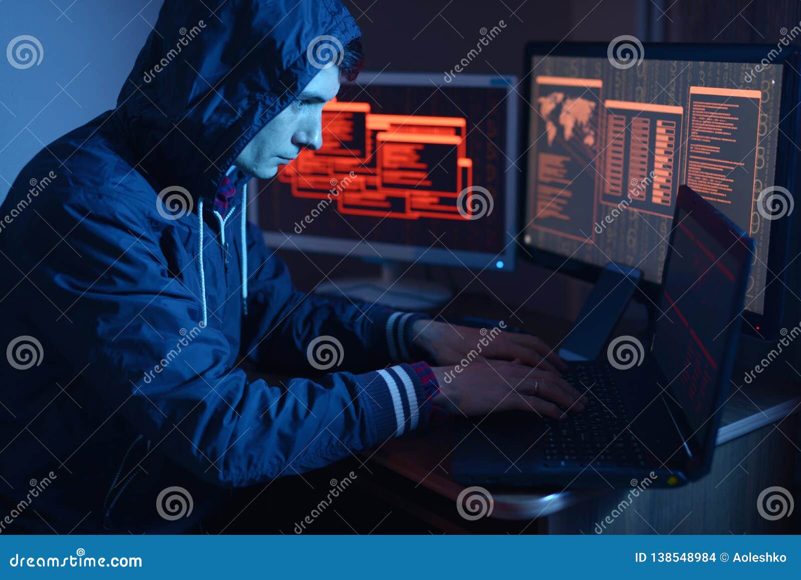 Hacker In A Hood Typing Program Code While Committing A Cybercrime On The Background Of Screens