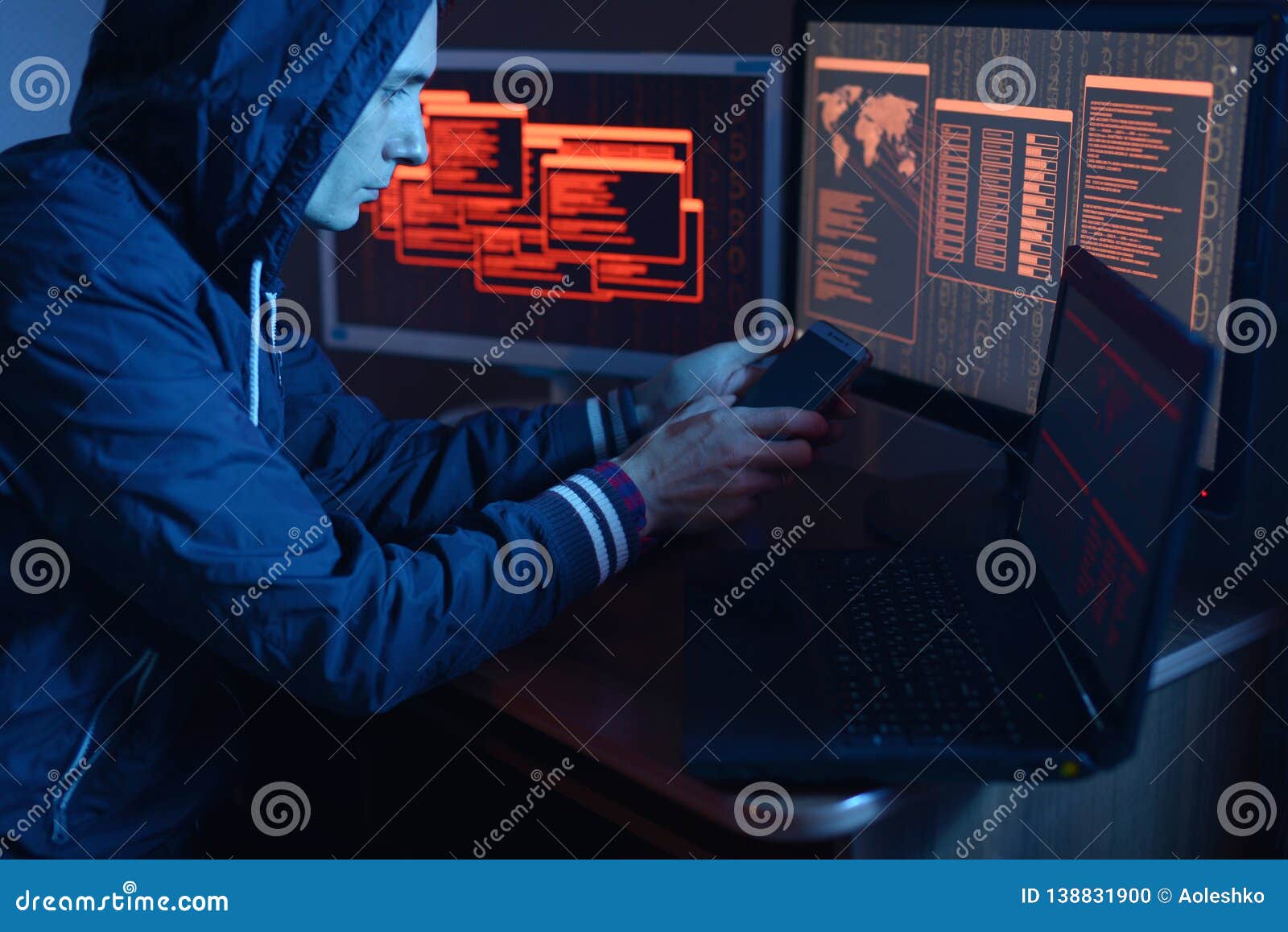 Hacker In A Hood Typing Program Code While Committing A Cybercrime On The Background Of Screens