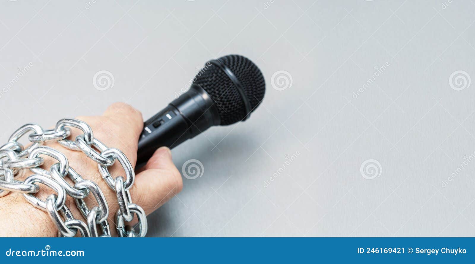 Male Hand Holding Microphone Tied With Chains On Grey Background With