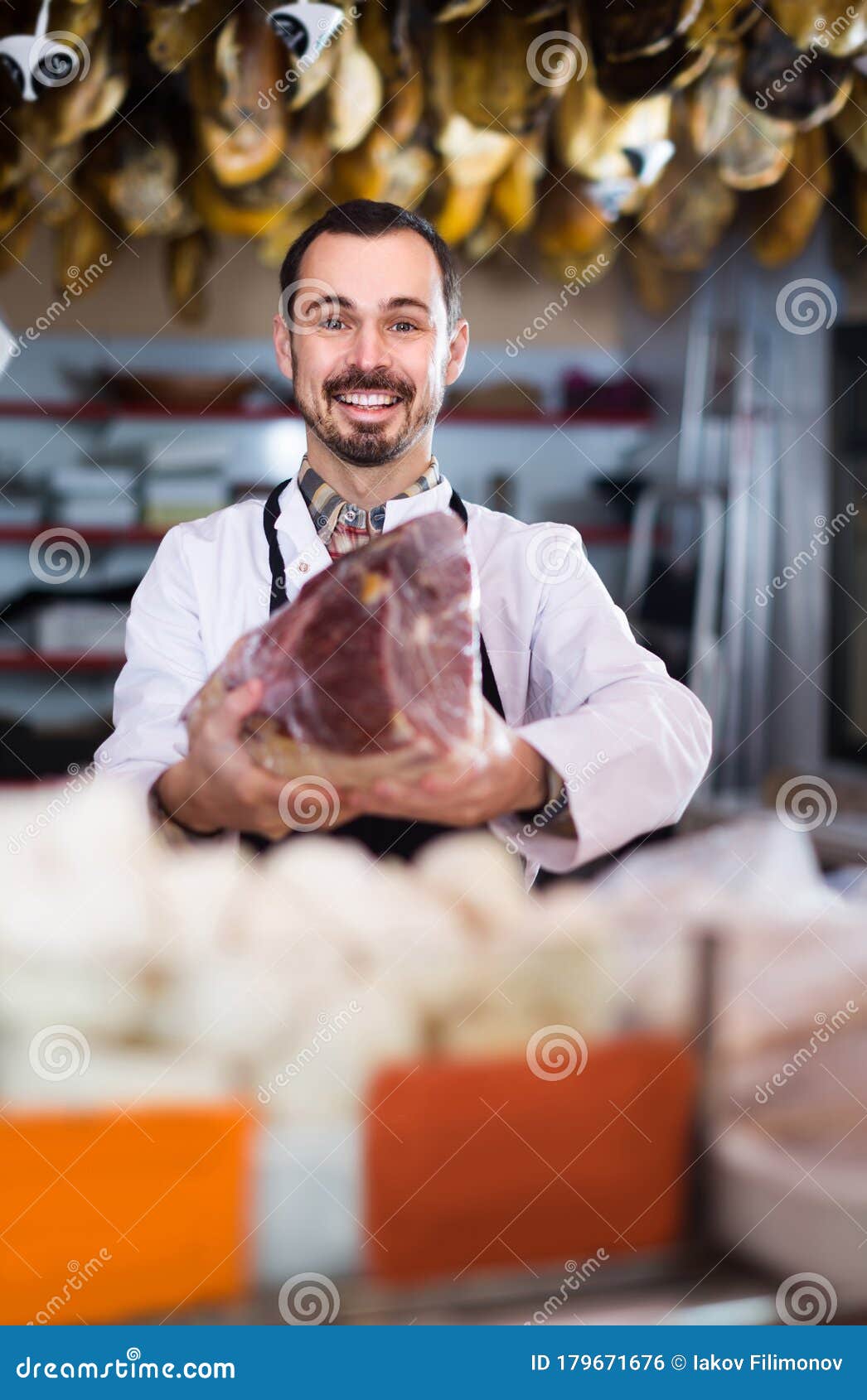 Male Shop Assistant Demonstrating Piece Of Meat In Butcher’s Shop