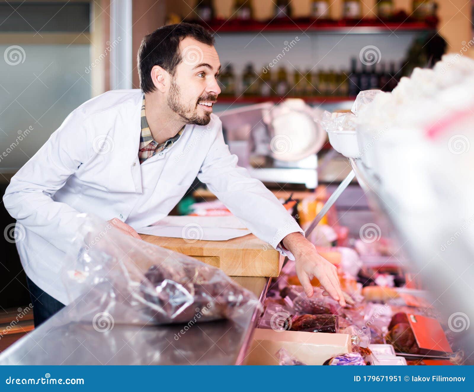 Male Shop Assistant Demonstrating Sliced Bacon In Butcher’s Shop
