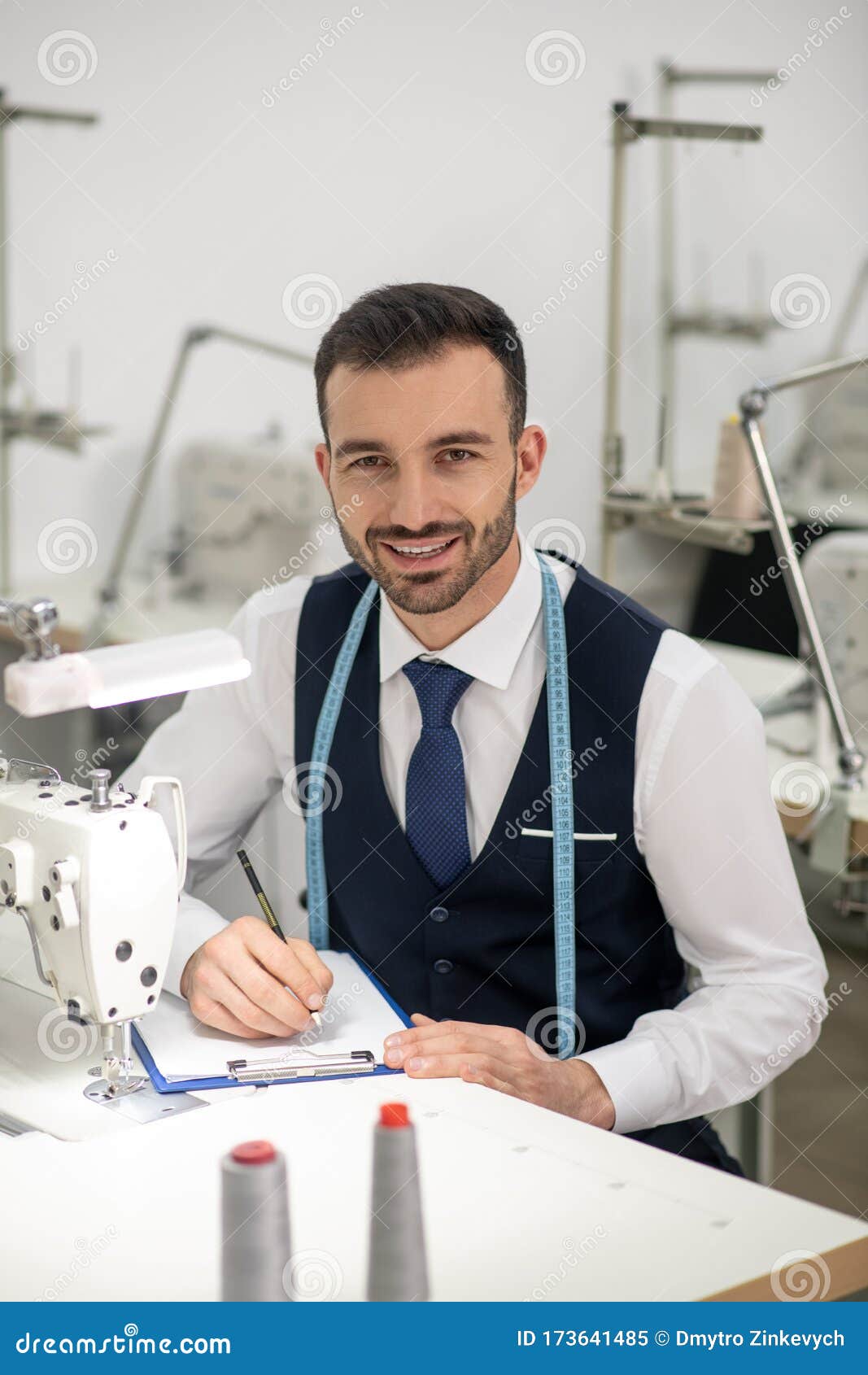 Male Tailor Sitting at Sewing Machine, Making Notes, Smiling Stock ...