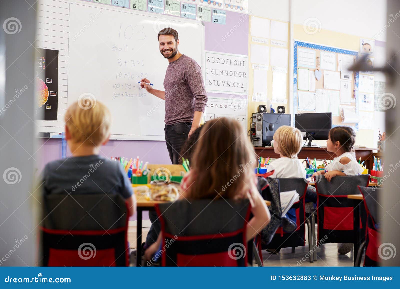 Male Teacher Standing at Whiteboard Teaching Maths Lesson To Elementary ...