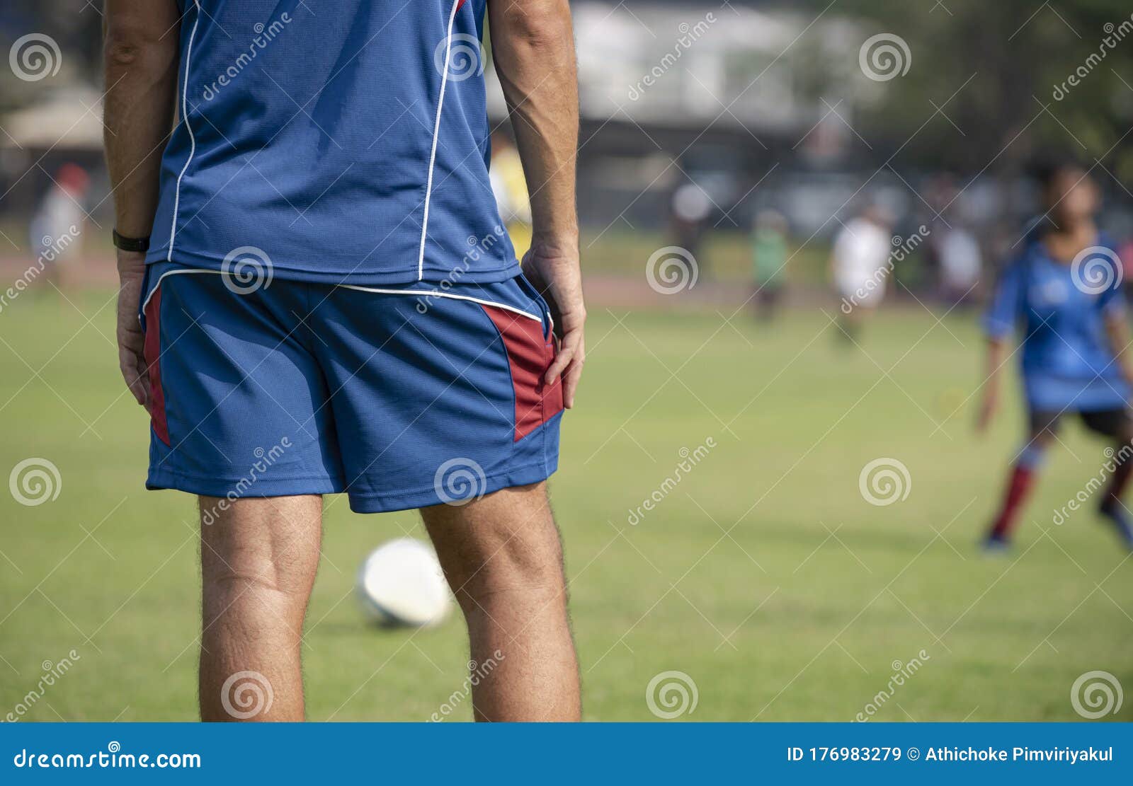 Male Youth Football Coach Standing And Watching His Team Playing In A School Tournament On A