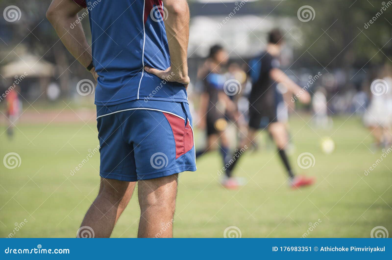 Male Youth Football Coach Standing And Watching His Team Playing In A School Tournament On A