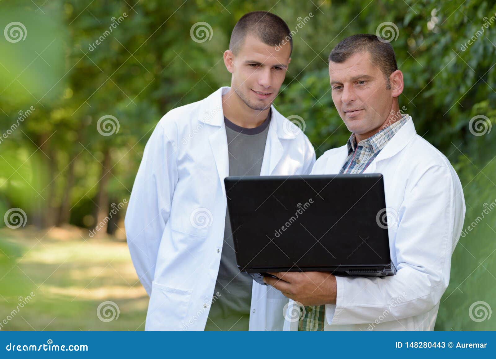 Man and Apprentice in White Coat Using Laptop Stock Image - Image of ...