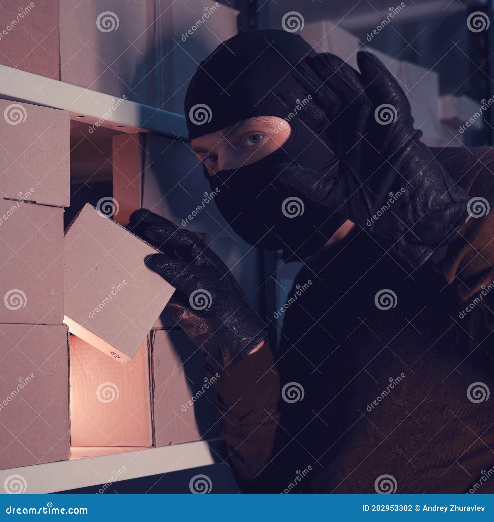 A Man in a Balaclava Steals a Box with a Parcel in a Warehouse at Night ...