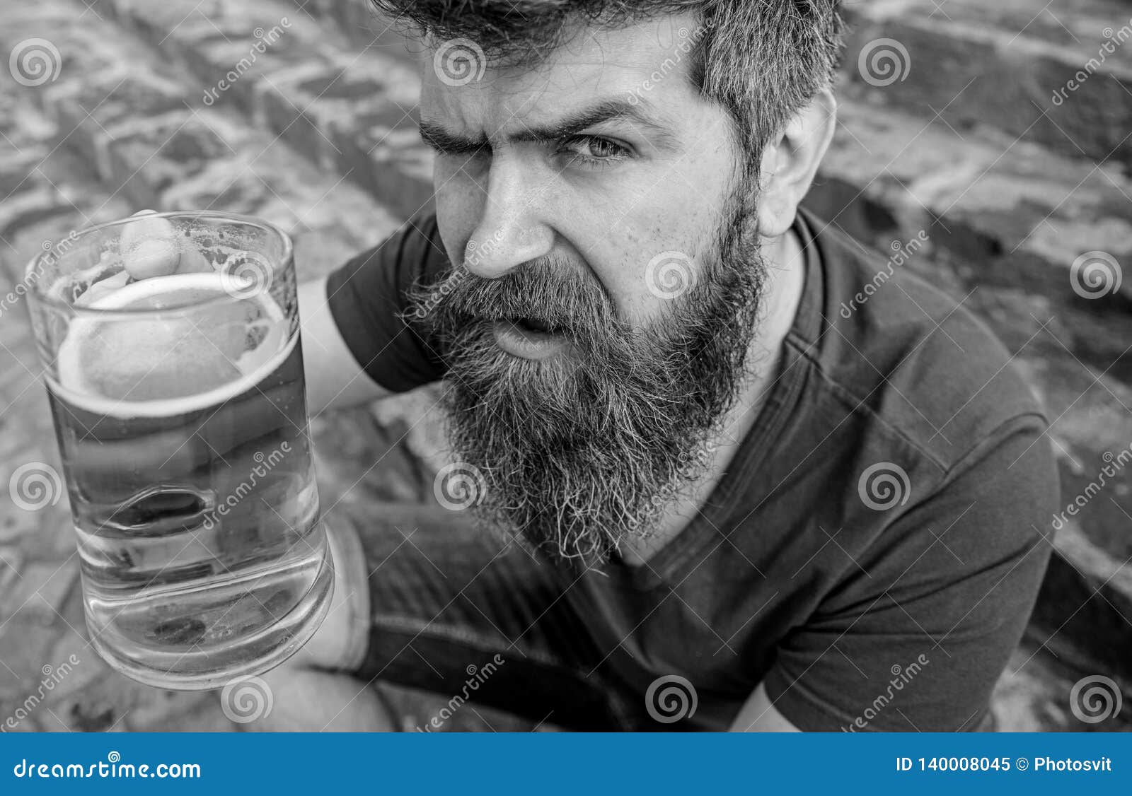 Man With Beard And Mustache Holds Glass With Beer While Sits On Stone