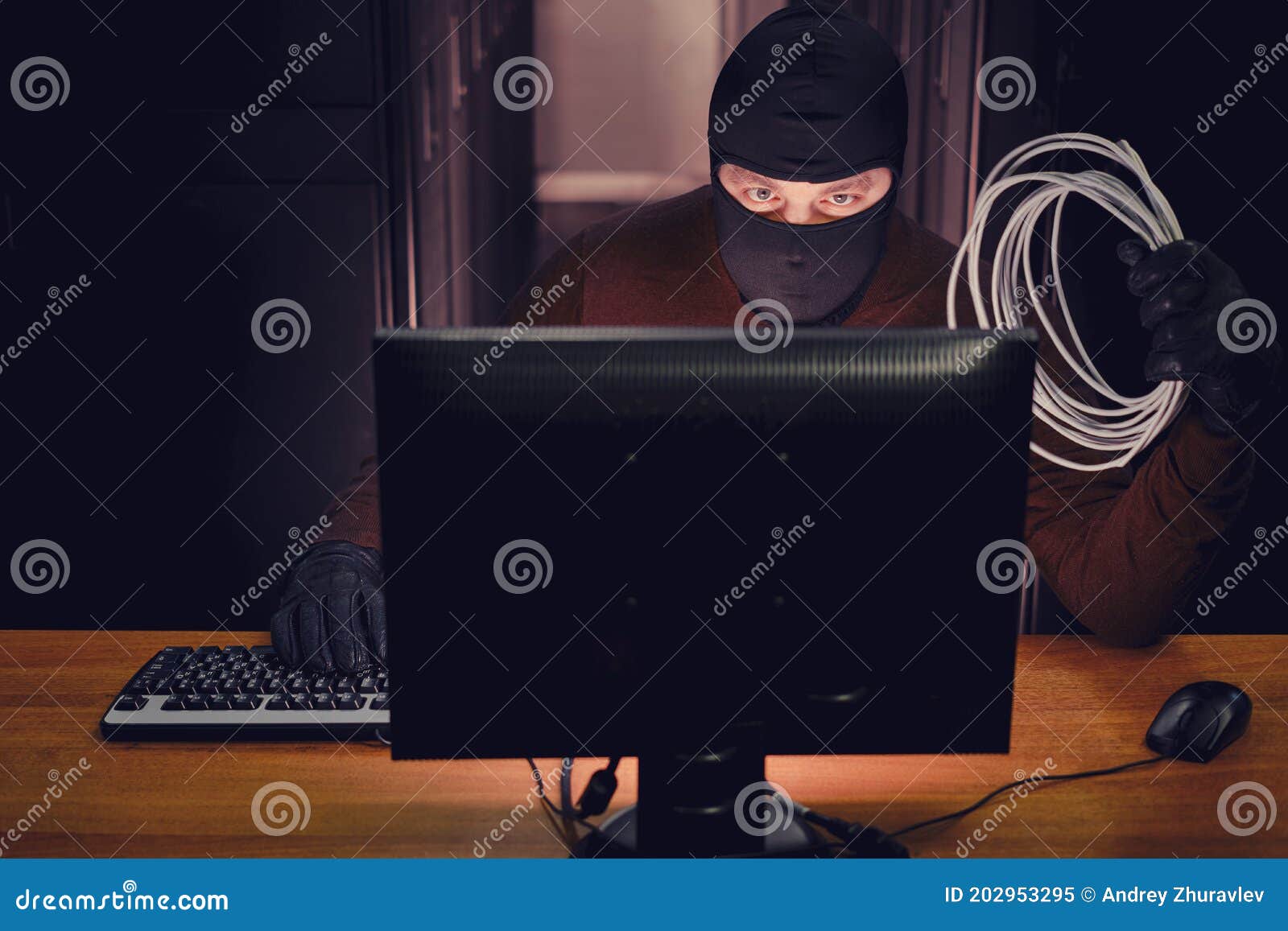 A Man in a Black Mask with Wires in His Hand Sits at a Computer in a ...