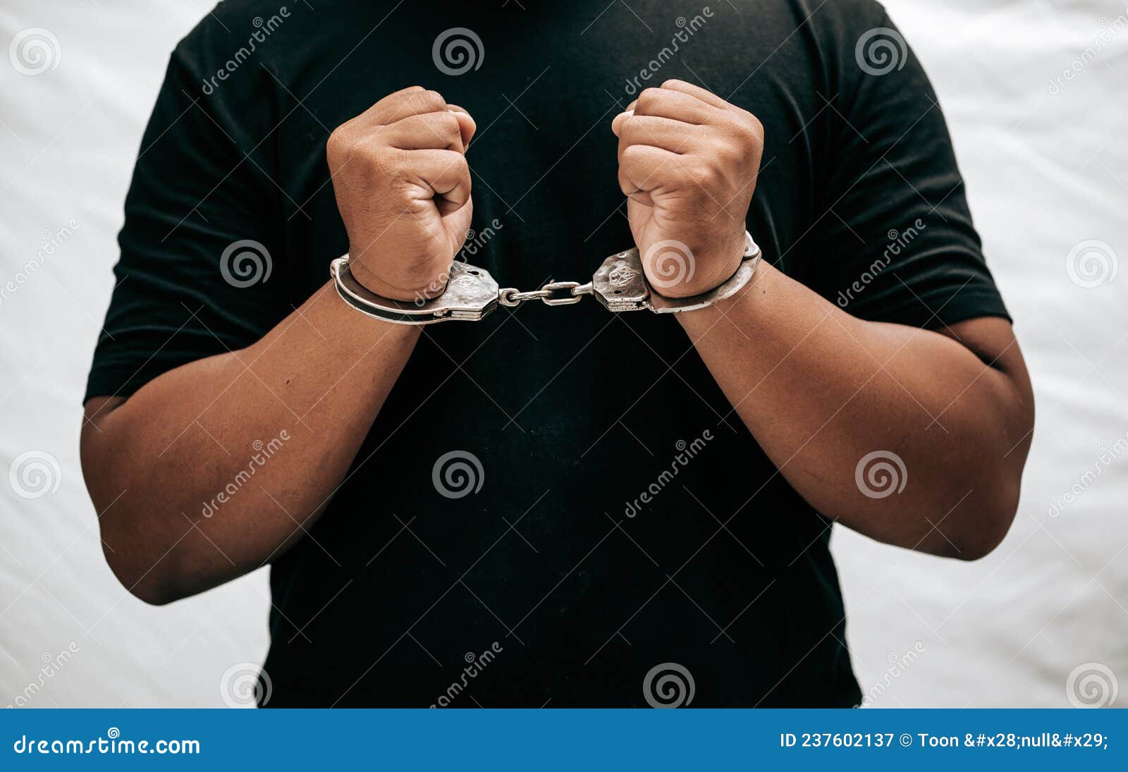 A Man in a Black Shirt Handcuffed from the Front on a White Background ...