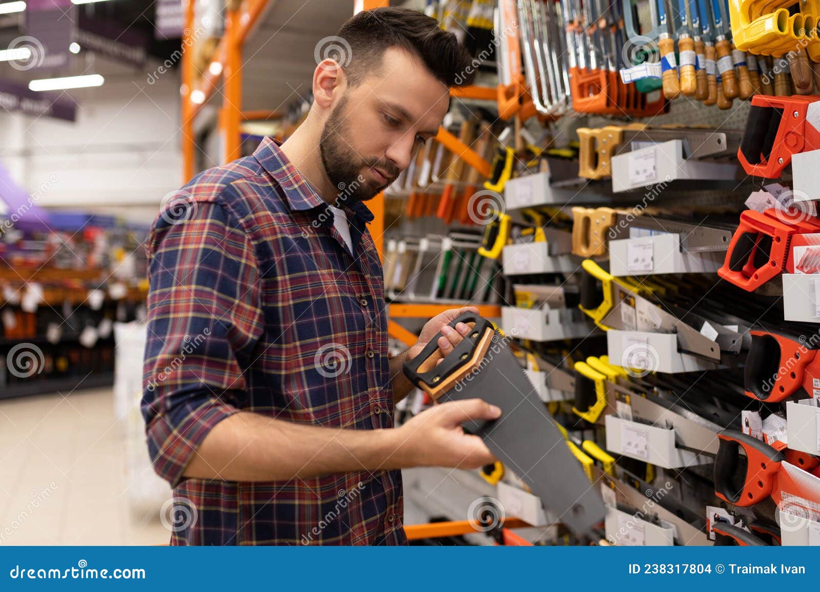A Man Builder at a Hardware Store Chooses a Hacksaw for Wood Next To a ...
