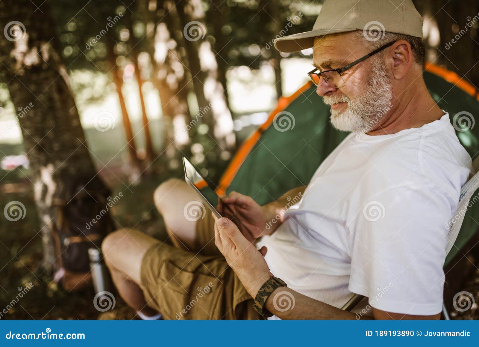 Man Camping in Nature Looking at Digital Tablet and Smiling Stock Photo ...
