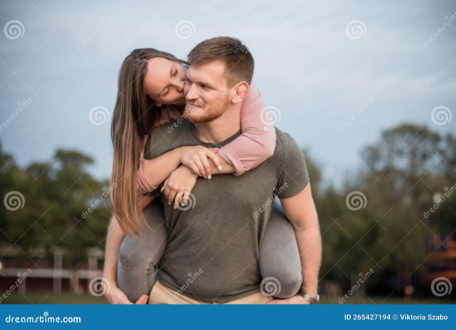 Man Carries His Girlfriend On His Back While She Kisses Him Stock