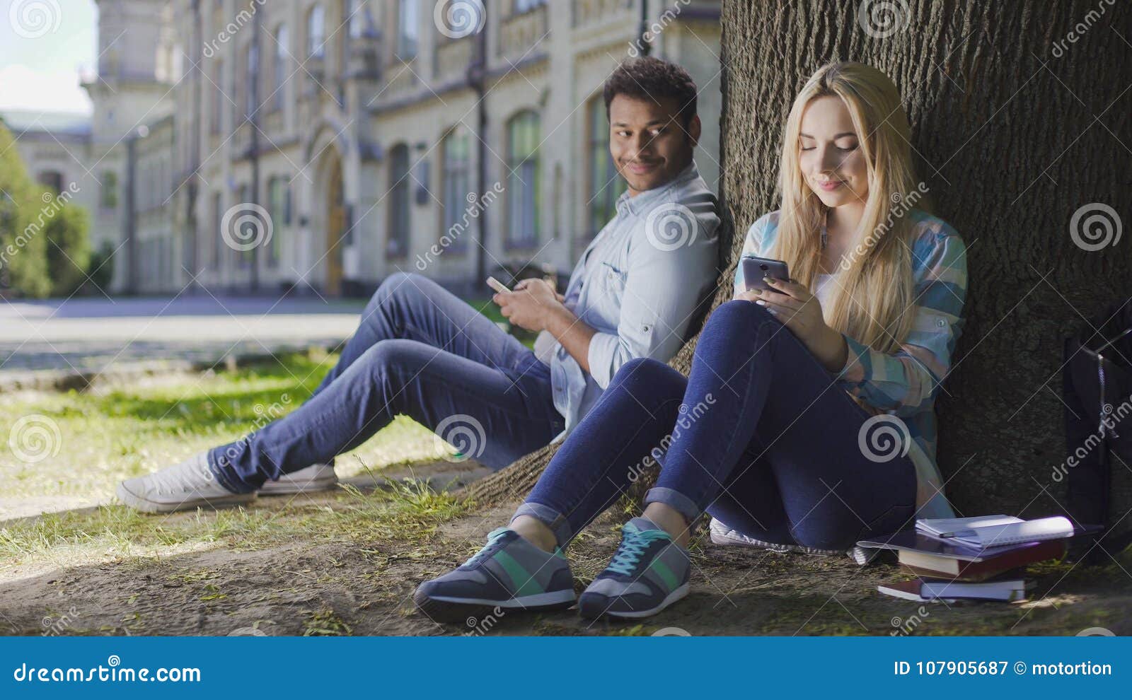 Man with Cellphone Sitting Under Tree and Looking at Girl Using Phone ...
