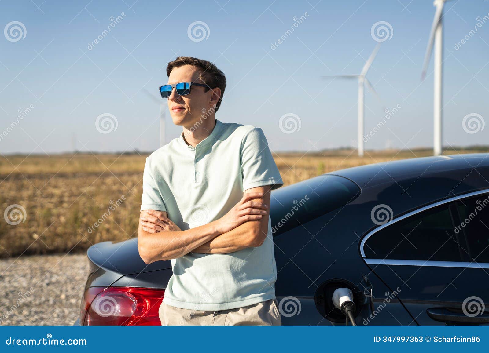 Man with Charging Electric Car. Wind Turbines in the Background Stock ...