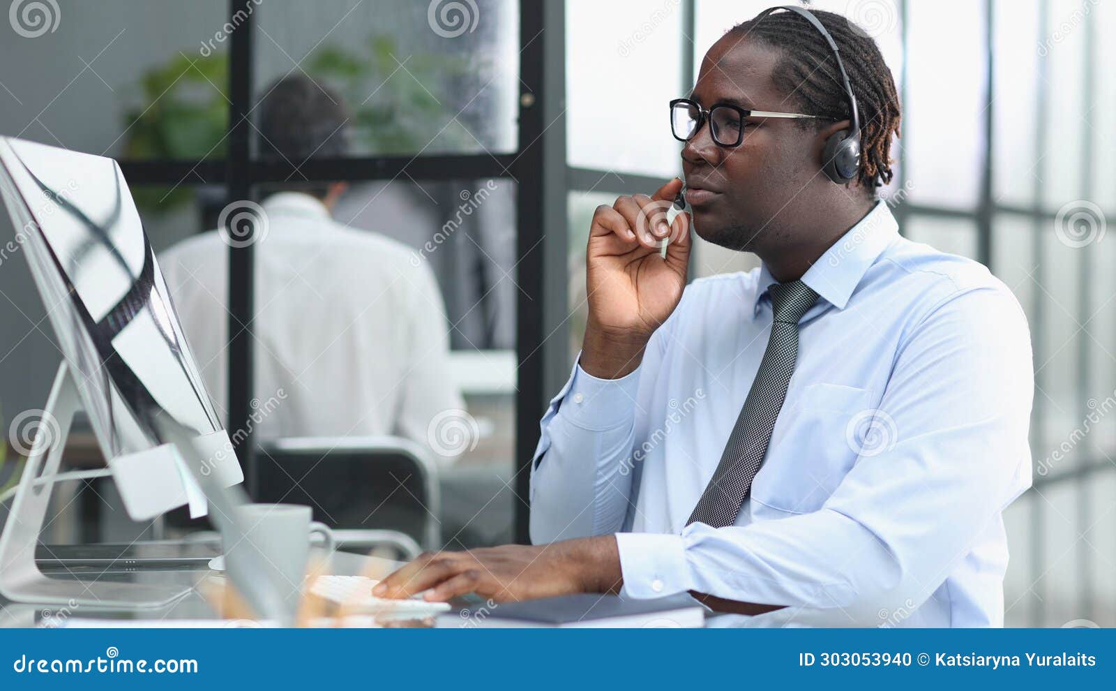 A Man at a Computer in a Call Center Talking Using Headphones with a ...