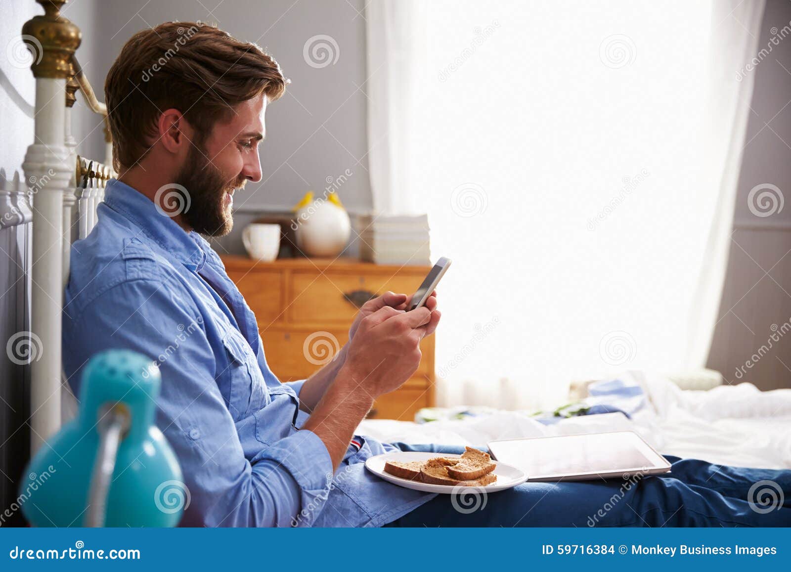 Man Eating Breakfast in Bed Whilst Using Mobile Phone Stock Photo ...