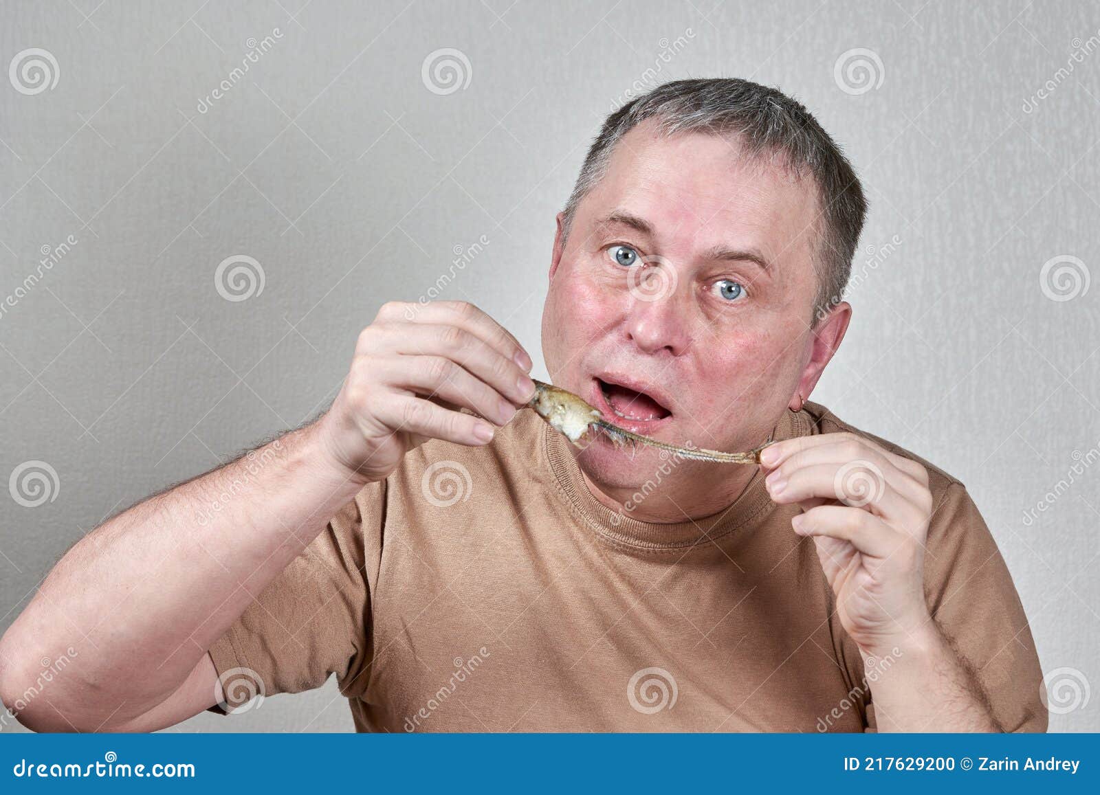 Man Eating Fried Smelt Fish Holding Fish with Hands in Front of Face ...