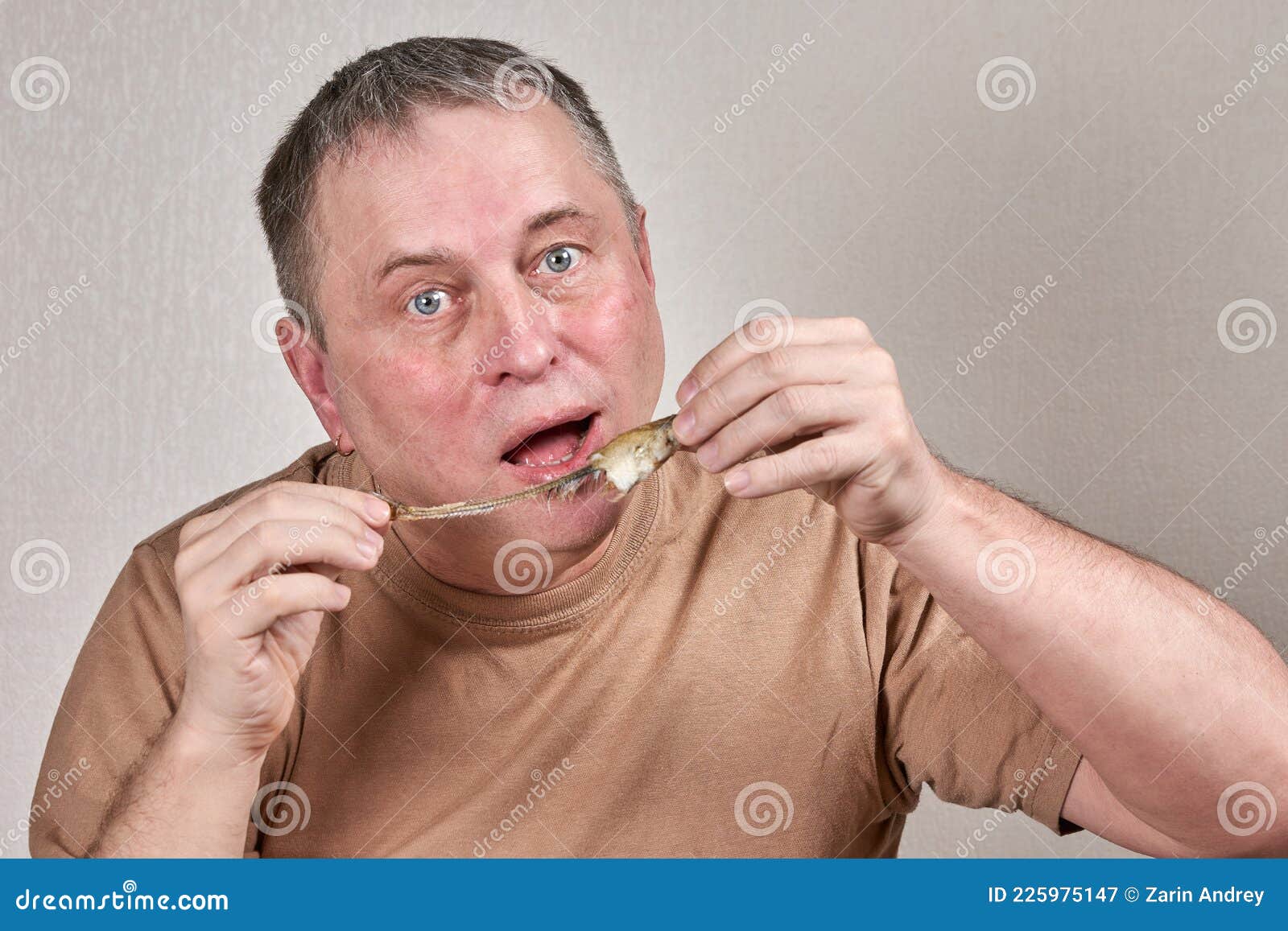 Man Eating Fried Smelt Fish Holding Fish with Hands in Front of Face ...