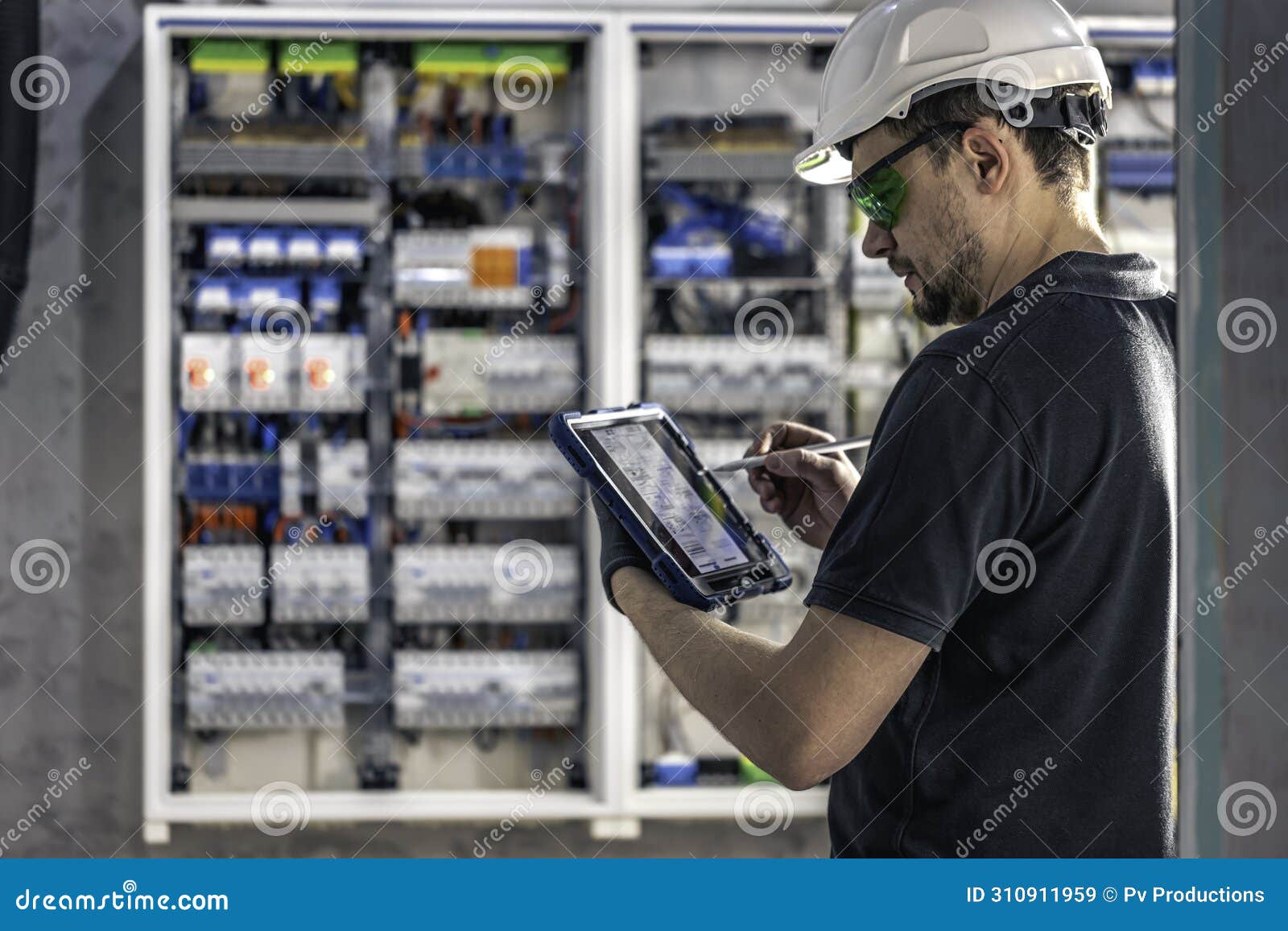 Man, an Electrical Working in a Switchboard with Fuses, Uses a Tablet ...