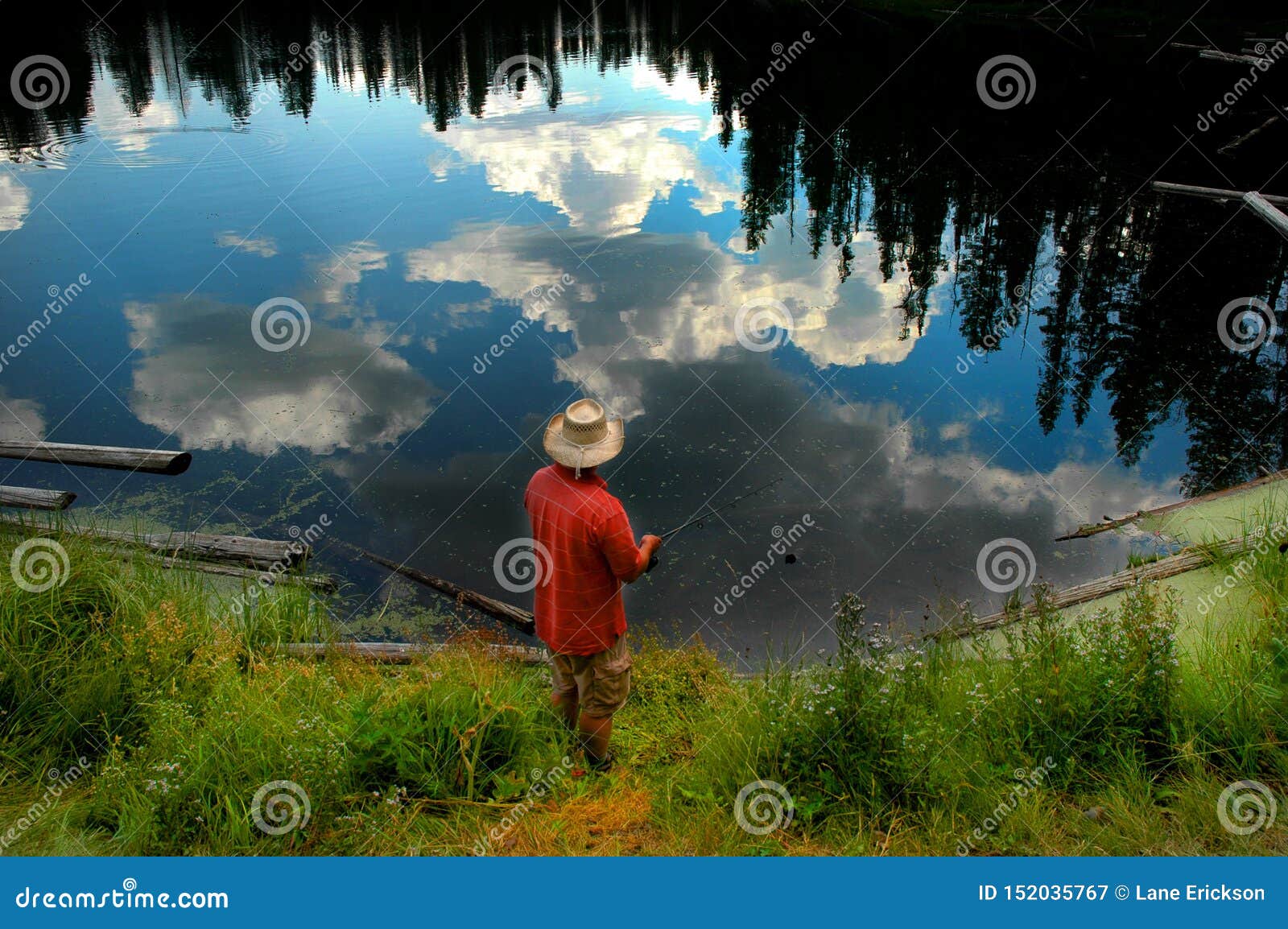 Man Fishing in Mountain Lake with Reflection of Trees Sky and Clouds ...