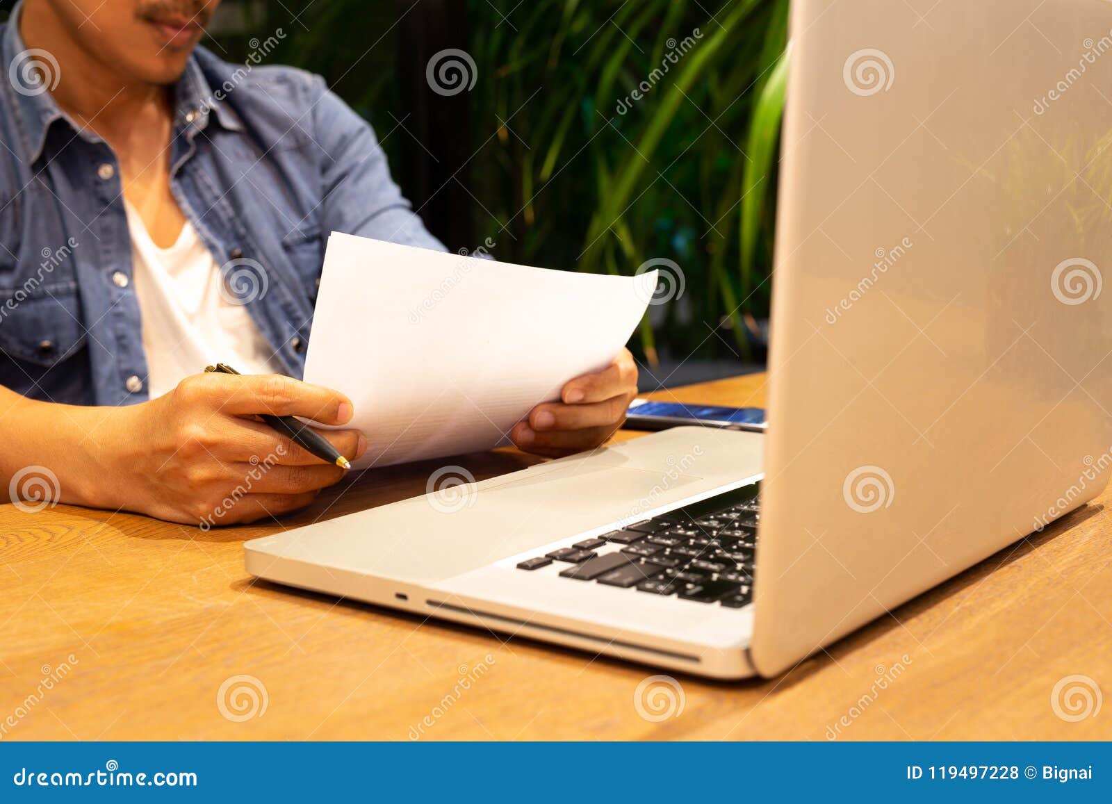 Man Hand Holding Pen Reading Paper Work with Laptop on Table Stock ...