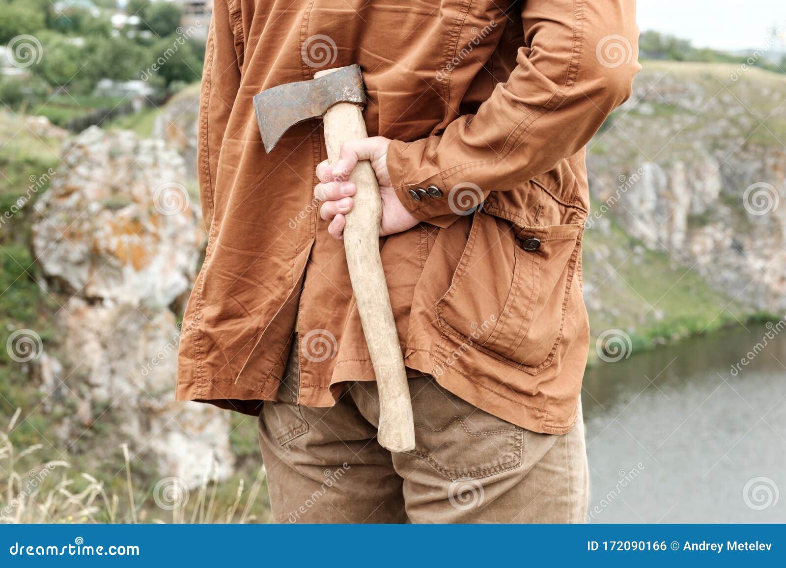 A Man Hides an Axe Behind His Back while Standing on the Bank of the ...