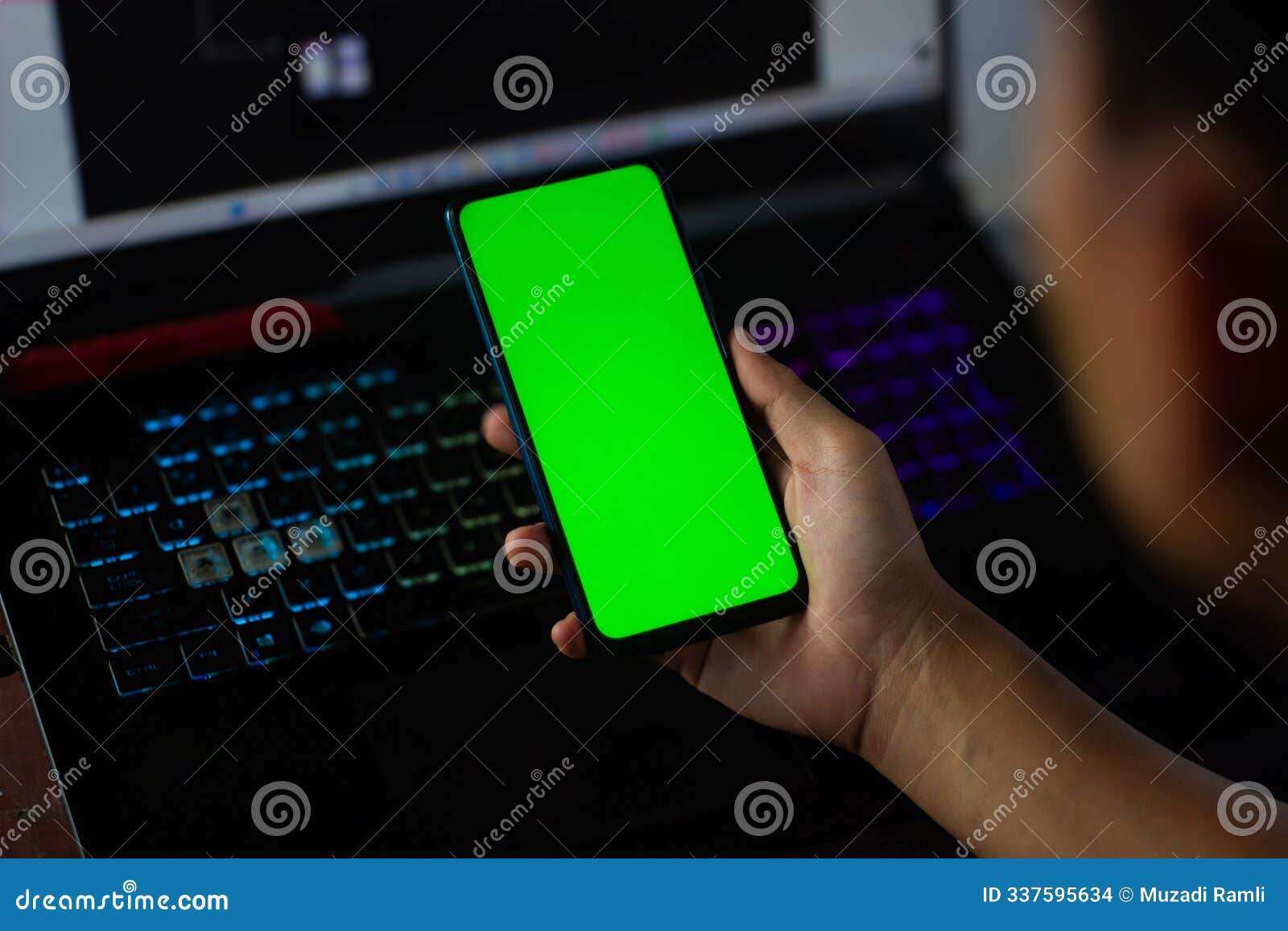 Man Holding Cell Phone with Bright Green Screen in Front of Laptop ...