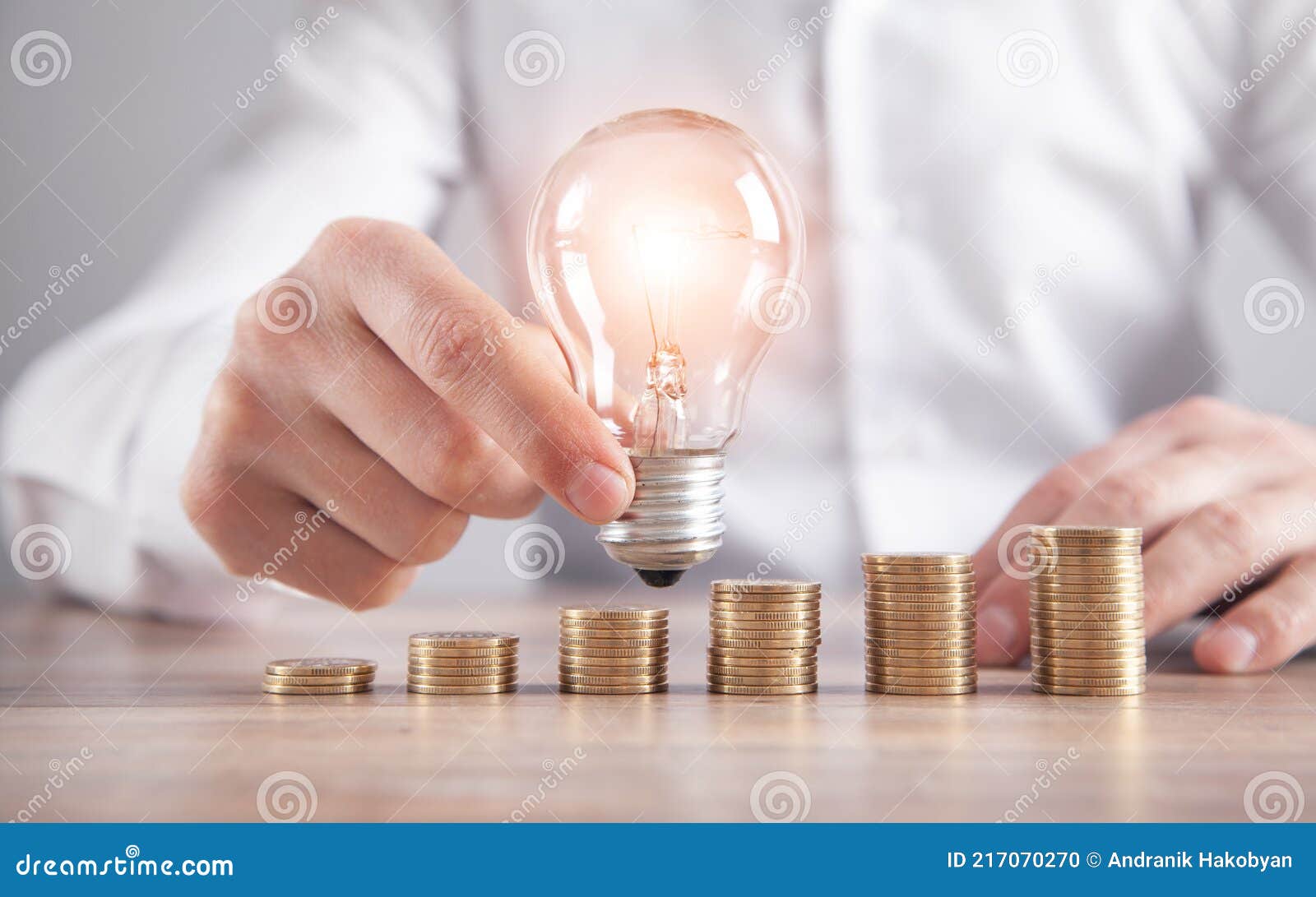Man Holding Light Bulb. Stack of Coins on the Desk Stock Photo - Image ...