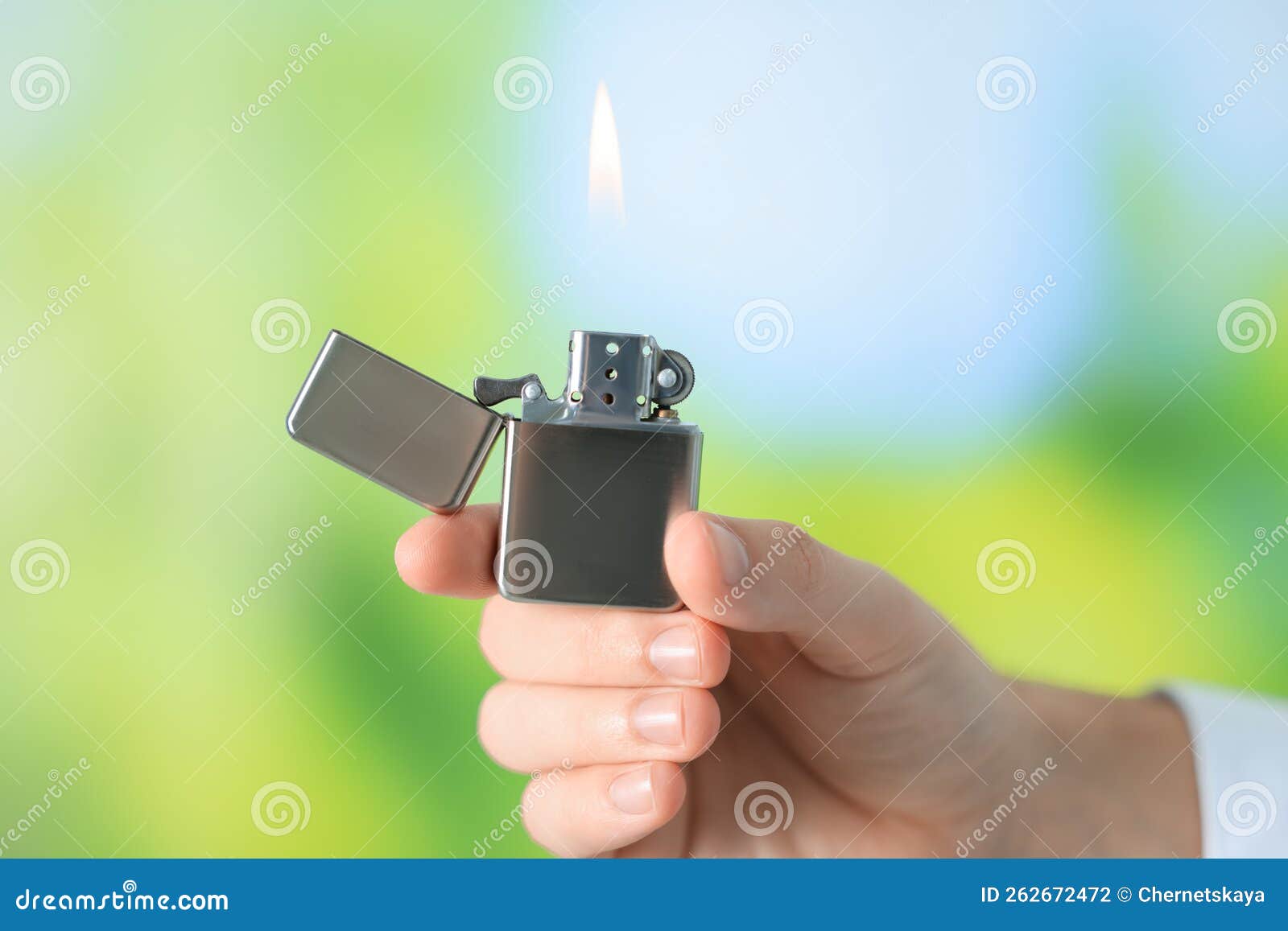 Man Holding Lighter with Burning Flame Against Blurred Green Background ...