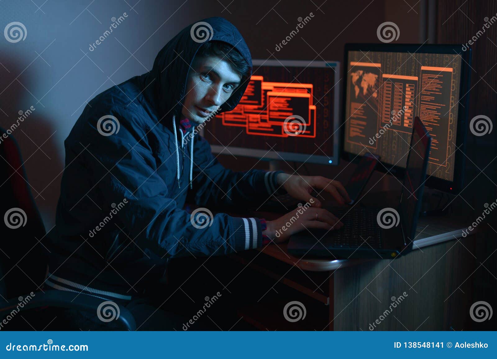 Man In The Hood Looking In The Camera Hacker Attacks And Online Fraud On The Screen Background