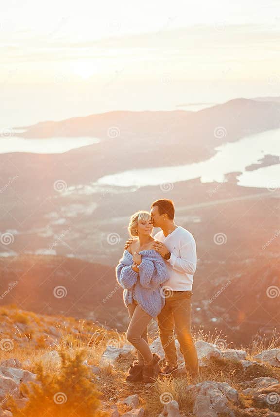Man Hugs A Woman From Behind And Kisses Her Temple While Standing On A