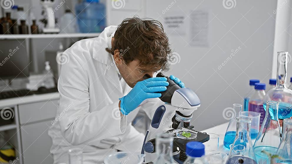 A Man in a Lab Coat Examines a Specimen Under a Microscope in a Well ...