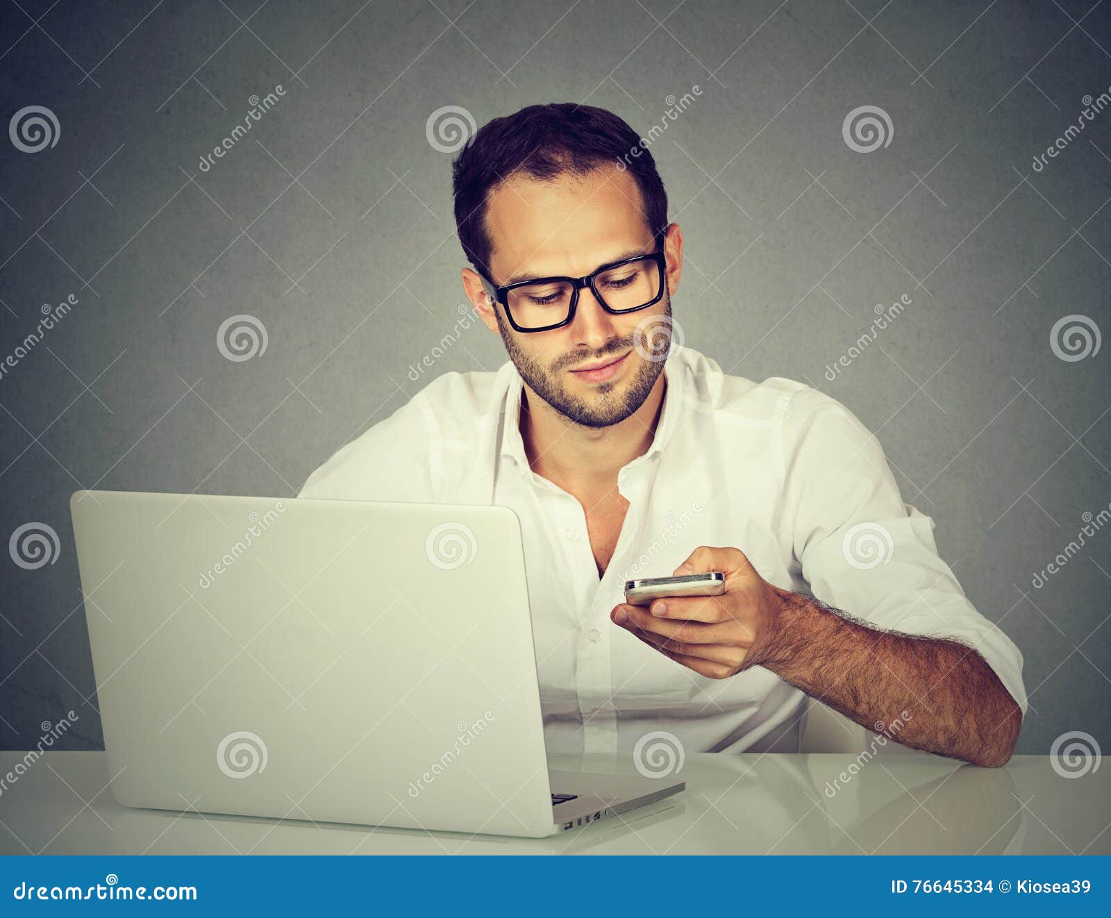 Man with Laptop Texting on Mobile Phone Sitting at Table Stock Photo ...