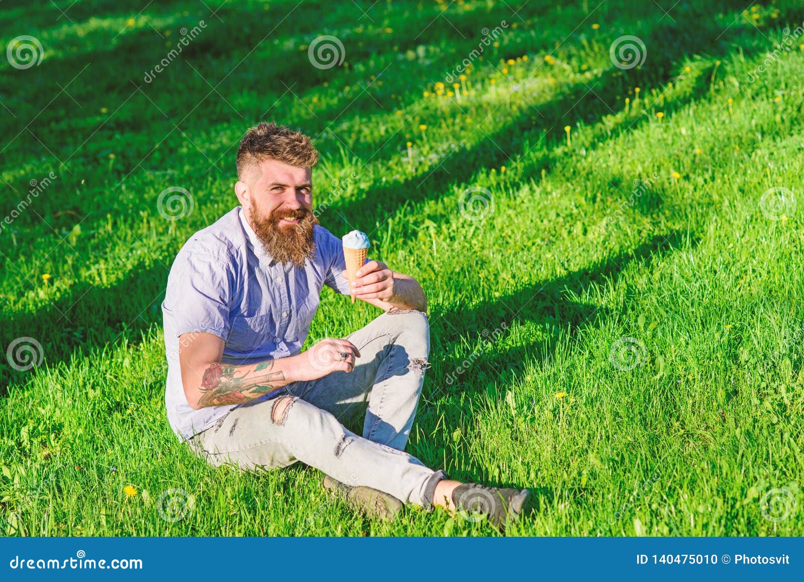 Man With Long Beard Enjoy Ice Cream While Sits On Grass Delicacy