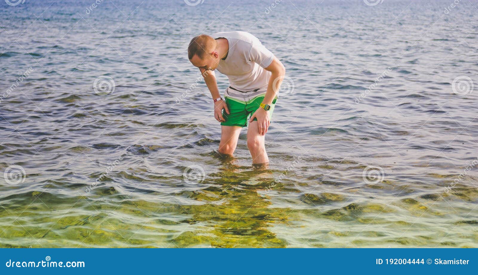 A Man Bending Over Looks at the Water, Studying the Seabed Stock Photo ...
