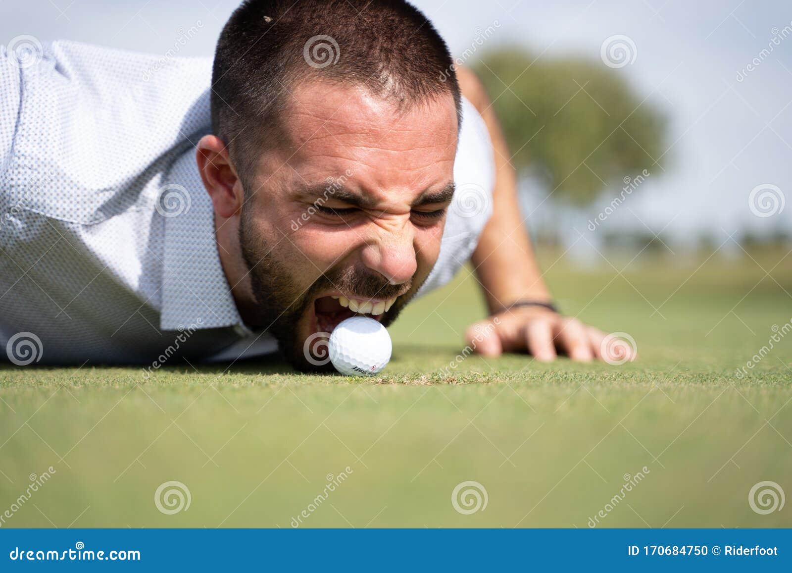 Man Lying on a Golf Course Biting a Golf Ball Next To a Hole Stock ...