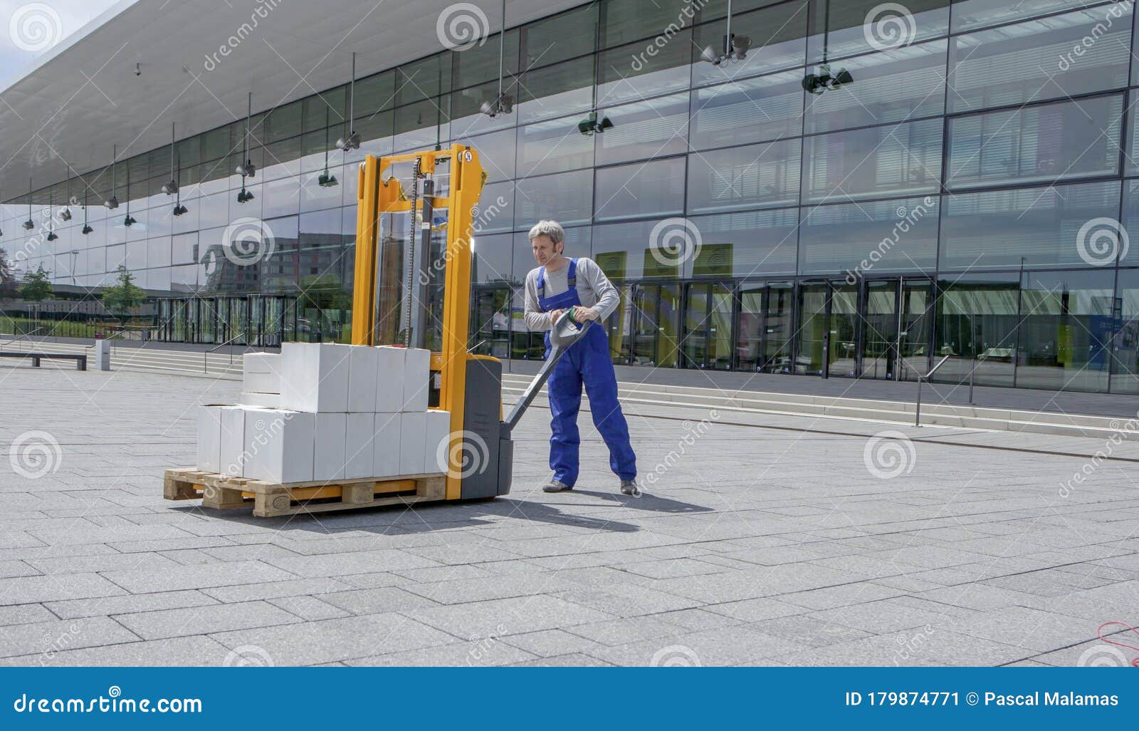 Man In Overalls Operates An Electric Stacker Loaded With Boxes Stock ...