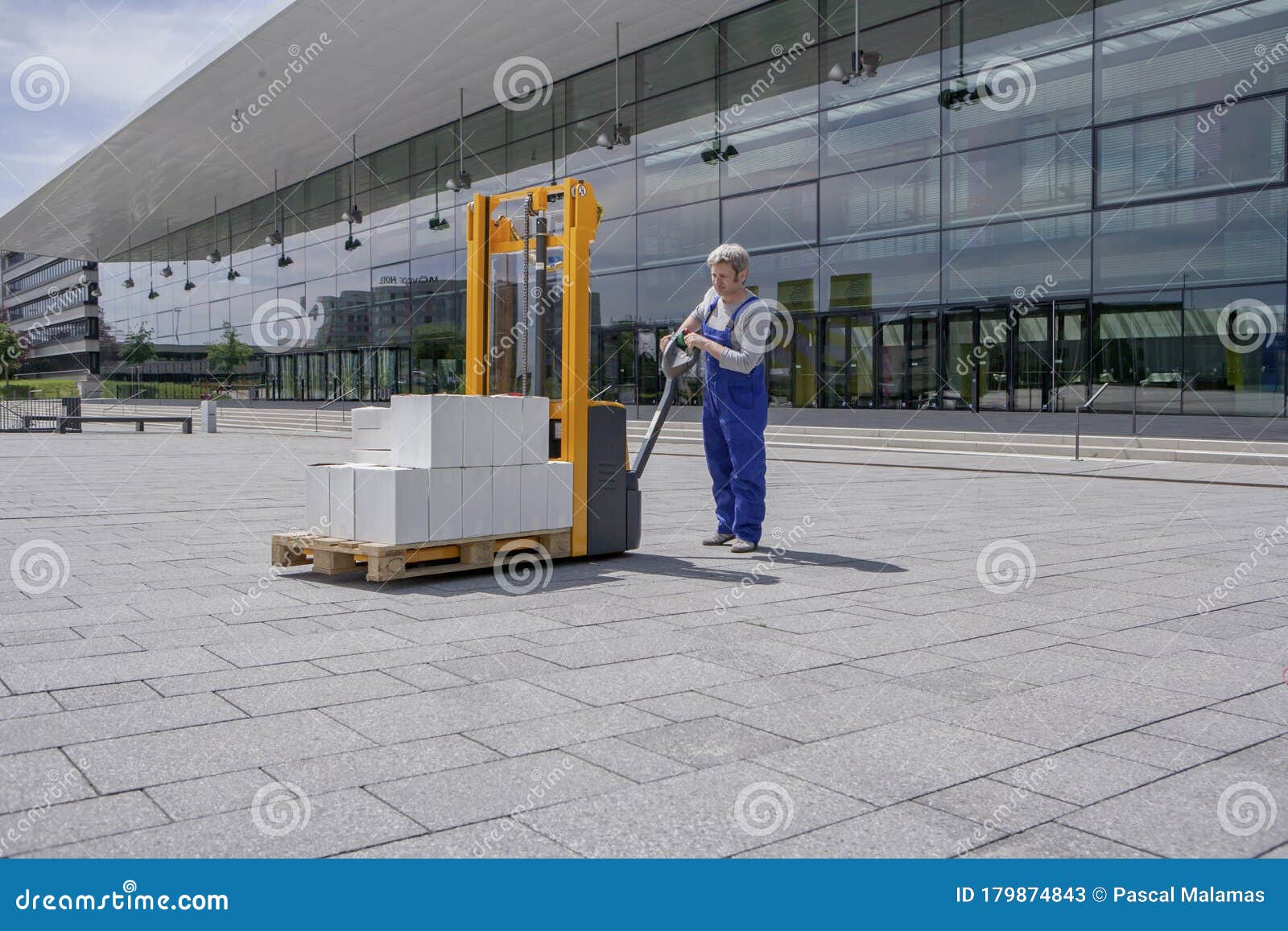 Man In Overalls Operates An Electric Stacker Loaded With Boxes Stock ...